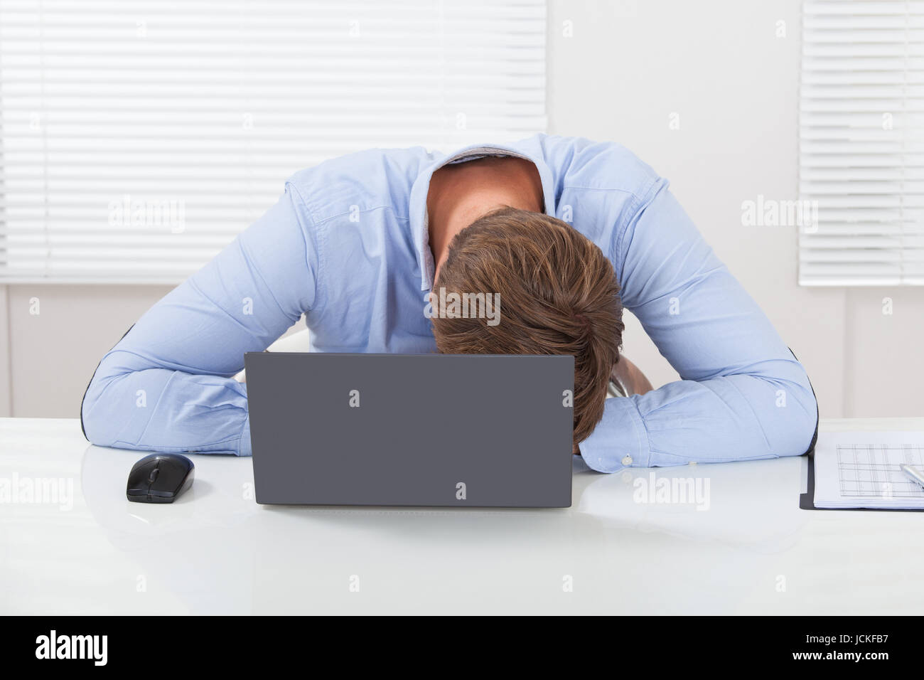Stressed businessman leaning on desk with laptop in office Stock Photo ...