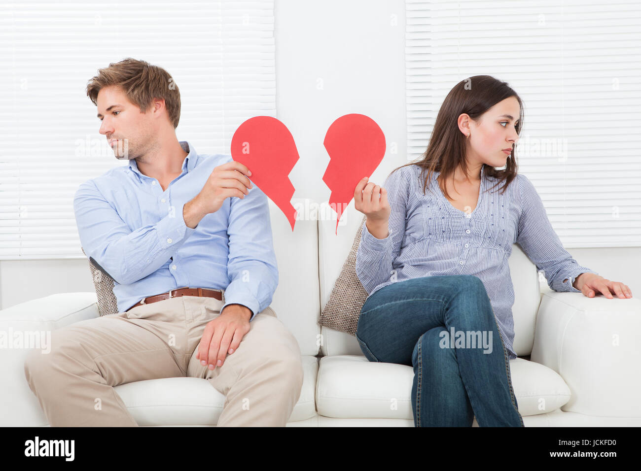 Full length of couple ignoring each other while sitting on sofa at home ...