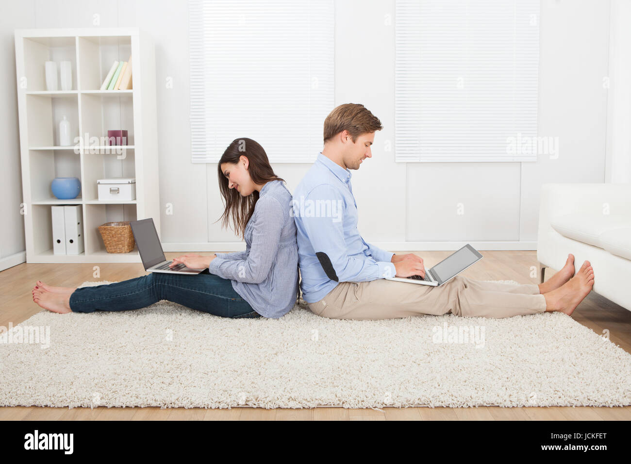 Full length of couple using laptops while sitting on rug in living room ...