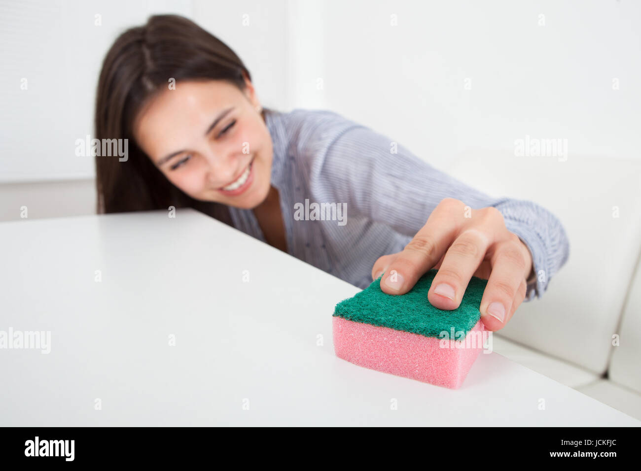 Happy young woman cleaning table with cleanser and rag in house Stock ...