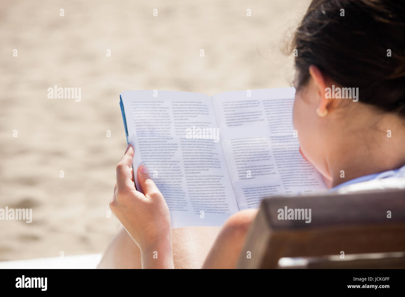 Rear view of woman reading book on deck chair at beach Stock Photo - Alamy