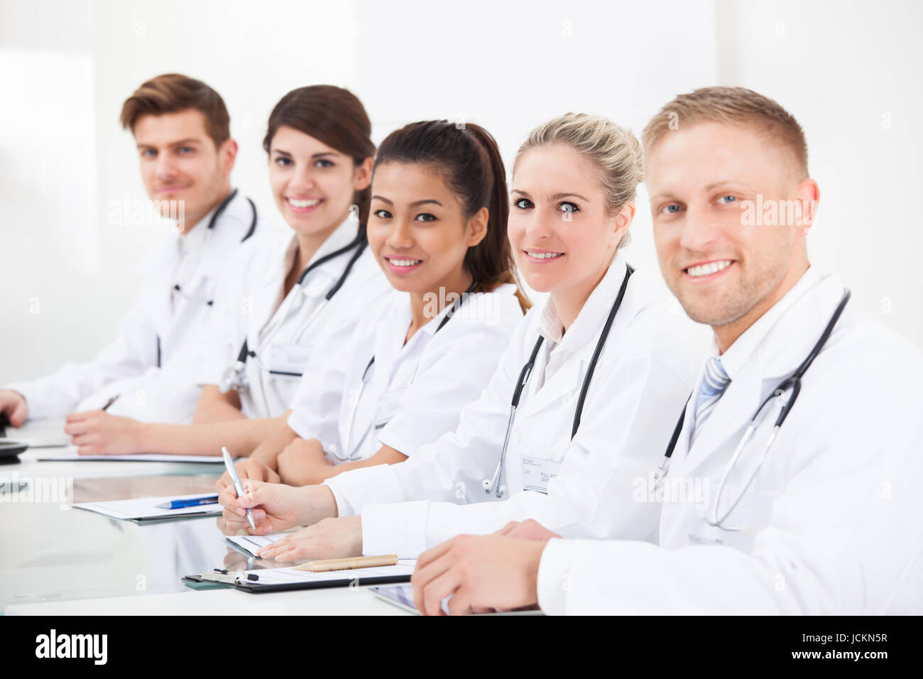 Portrait of confident doctors sitting in a row at desk Stock Photo - Alamy