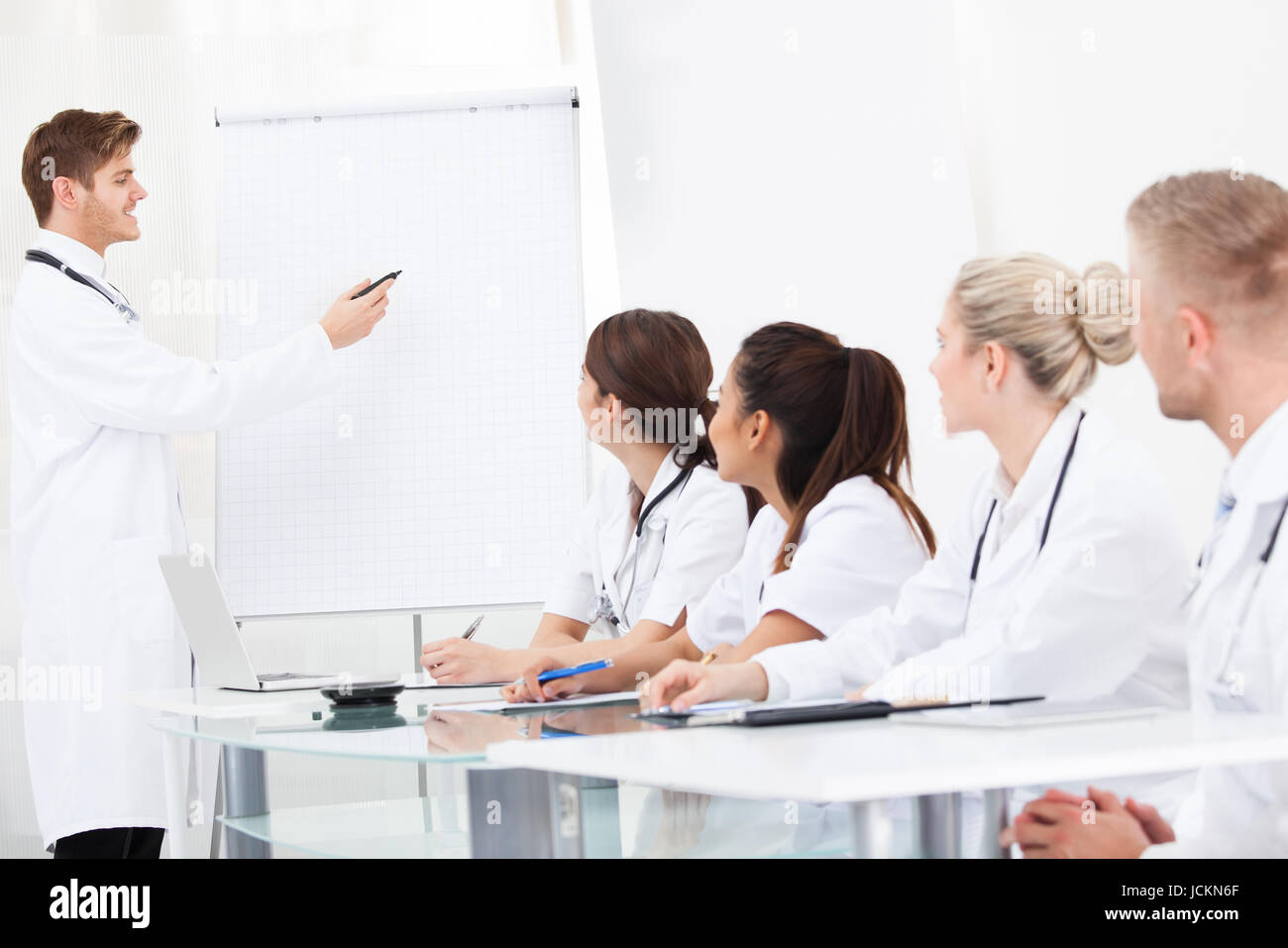 Young male doctor giving presentation to colleagues on flipchart in ...