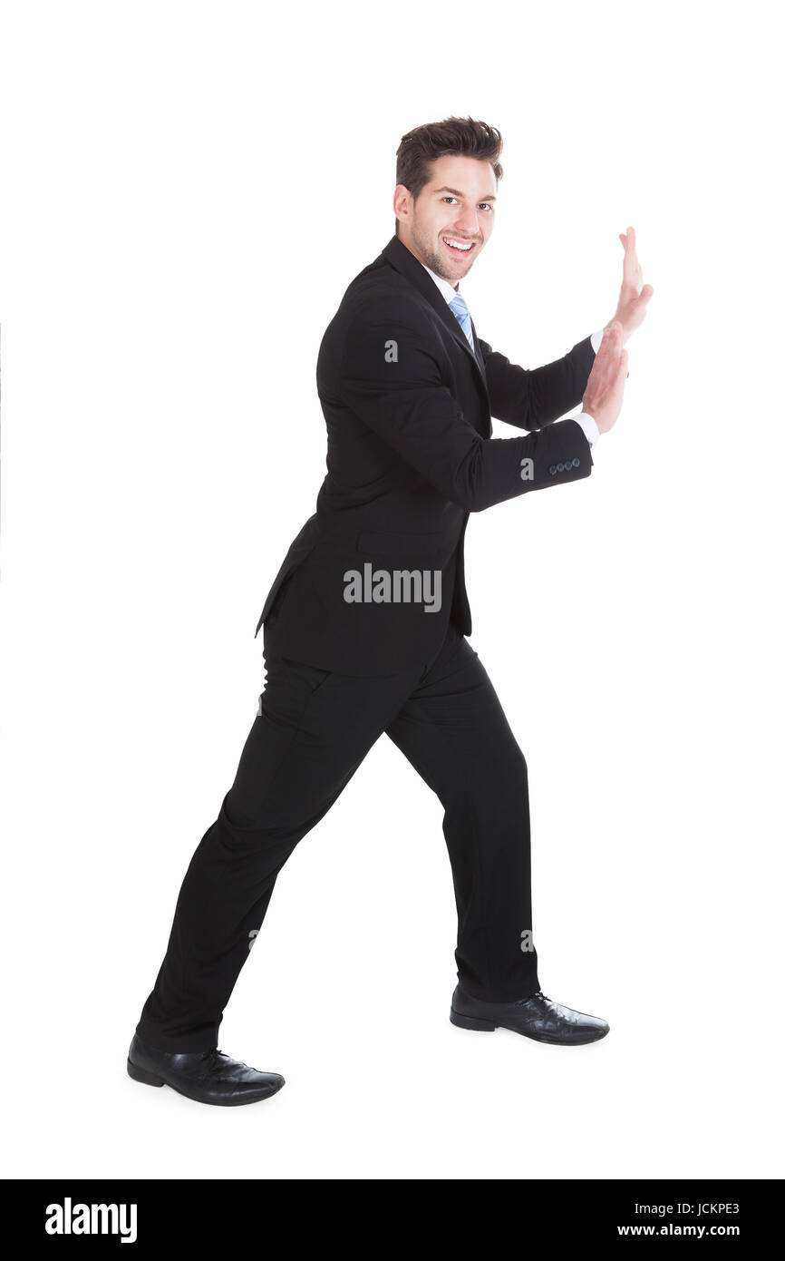 Full length side view of young businessman pushing something over white ...