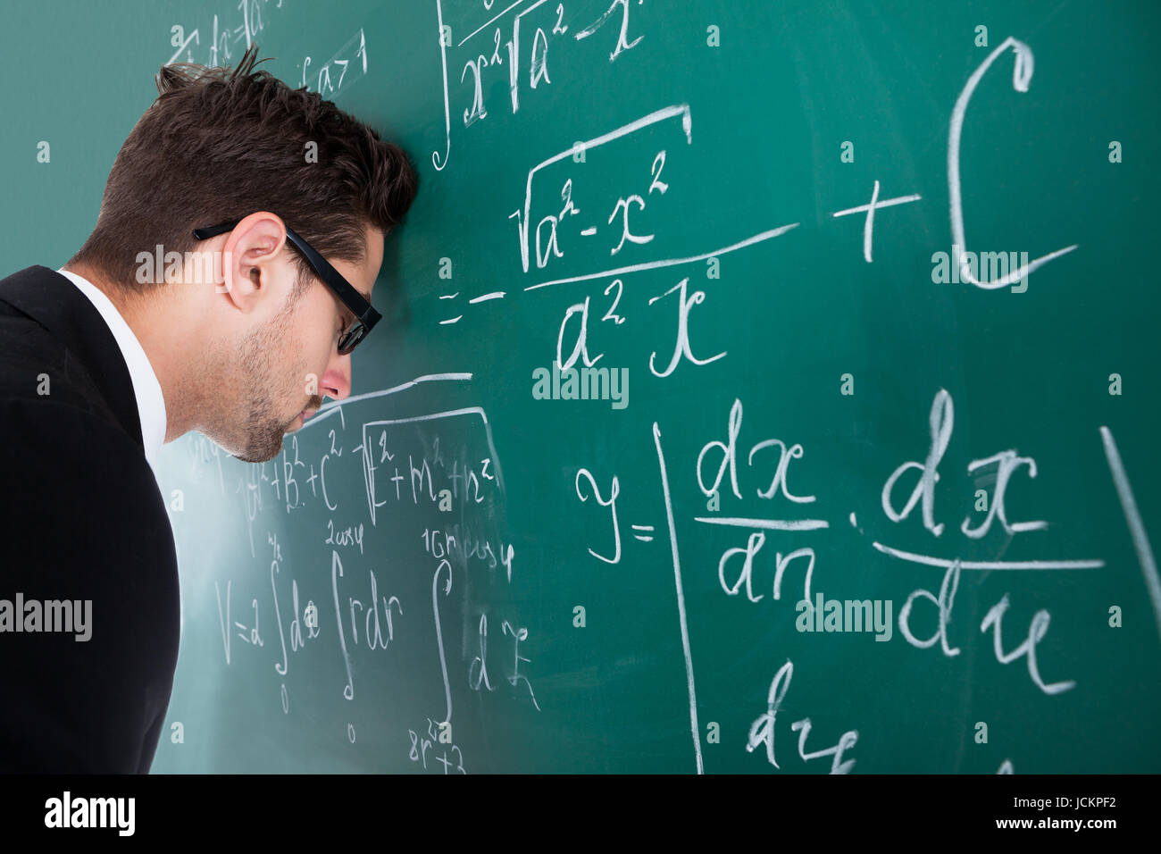 Side view of sad young male professor leaning head on blackboard in ...