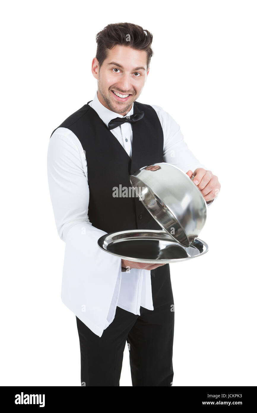 Portrait of butler lifting cloche from serving tray over white ...