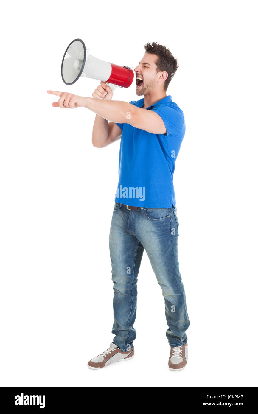 Full length of aggressive young man screaming into bullhorn while ...