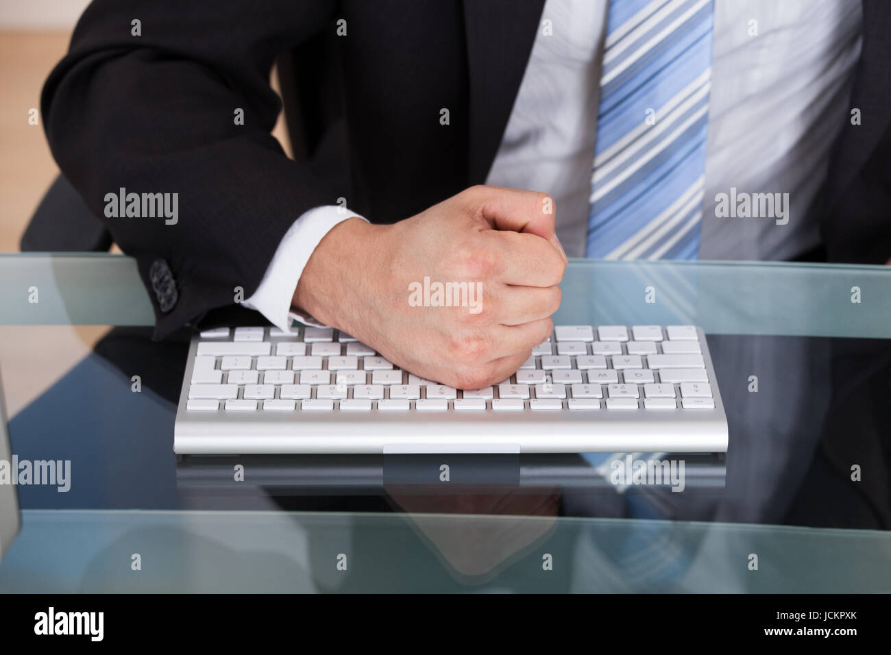 Midsection of businessman pounding fist on keyboard at office desk ...
