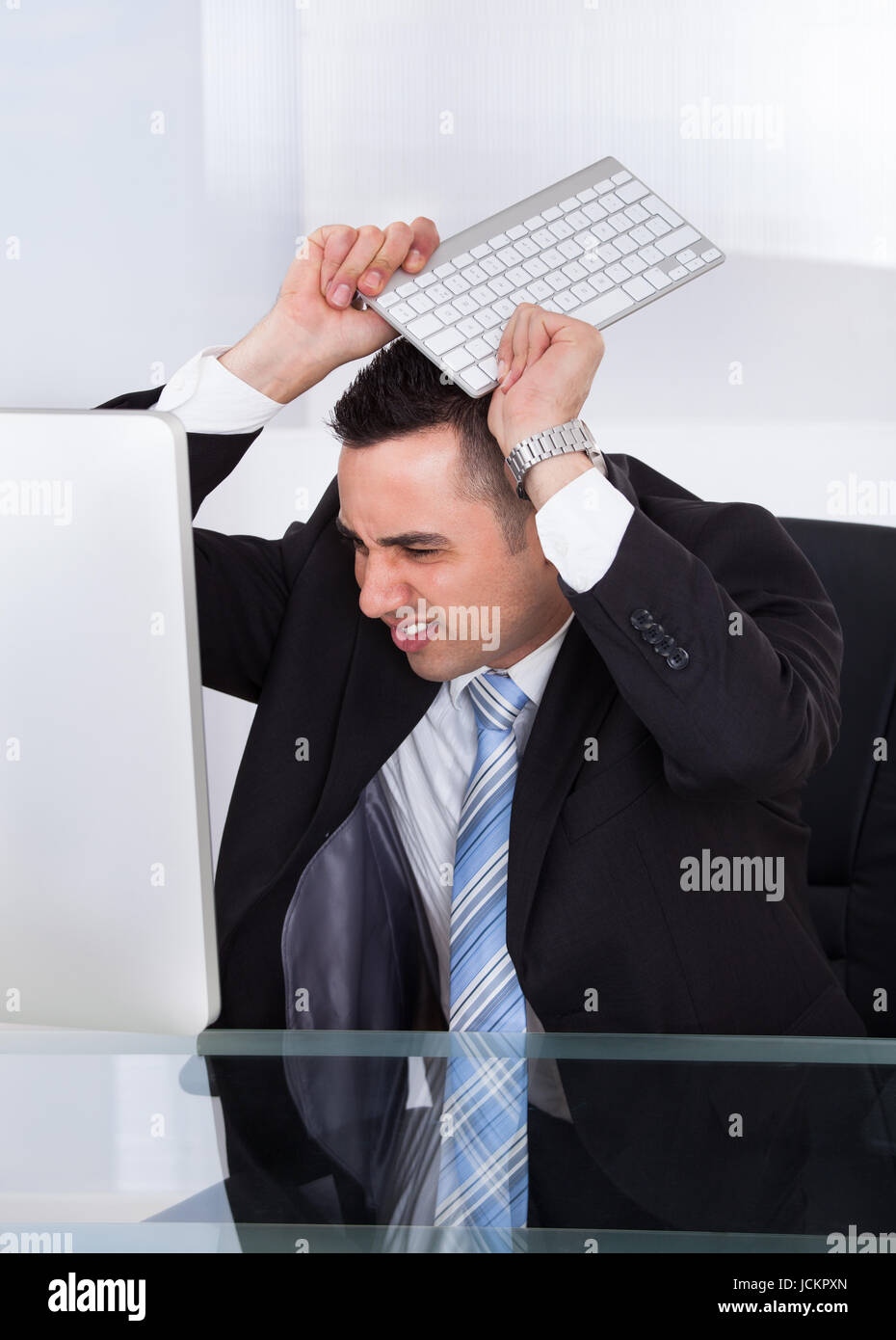 Frustrated young businessman throwing computer keyboard at office desk ...