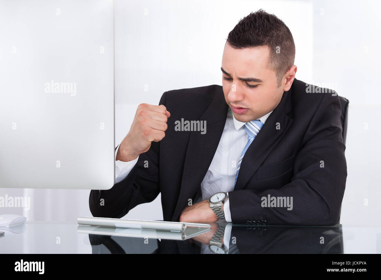 Stressed young businessman clenching fist at computer desk in office ...