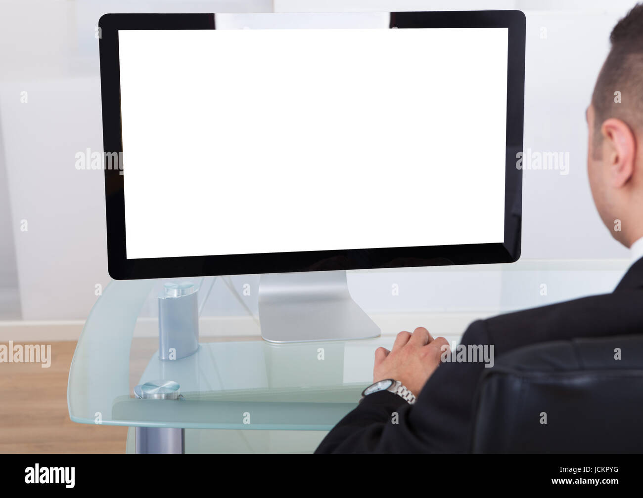 Rear view of young businessman using computer at office desk Stock ...