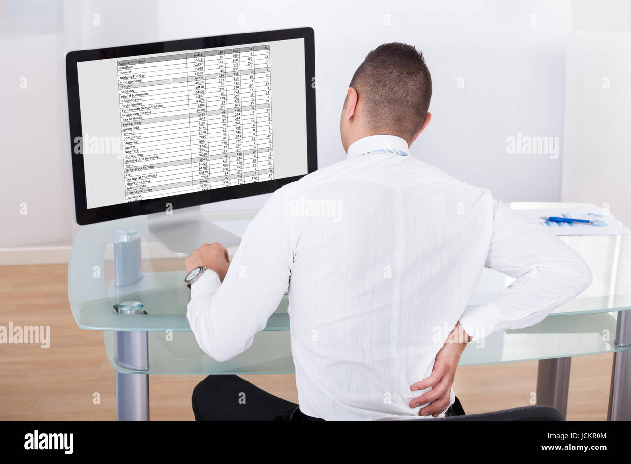Rear view of young businessman with backache using computer at office ...
