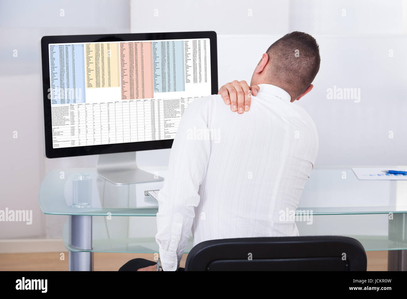 Rear view of young businessman with shoulder pain using computer at ...