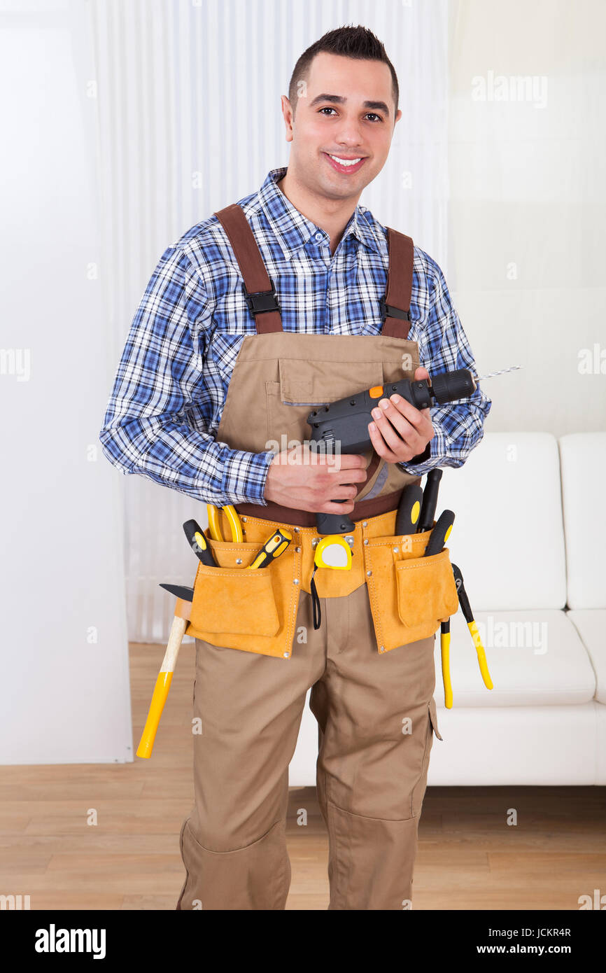 Full length portrait of confident male repairman holding drill machine ...