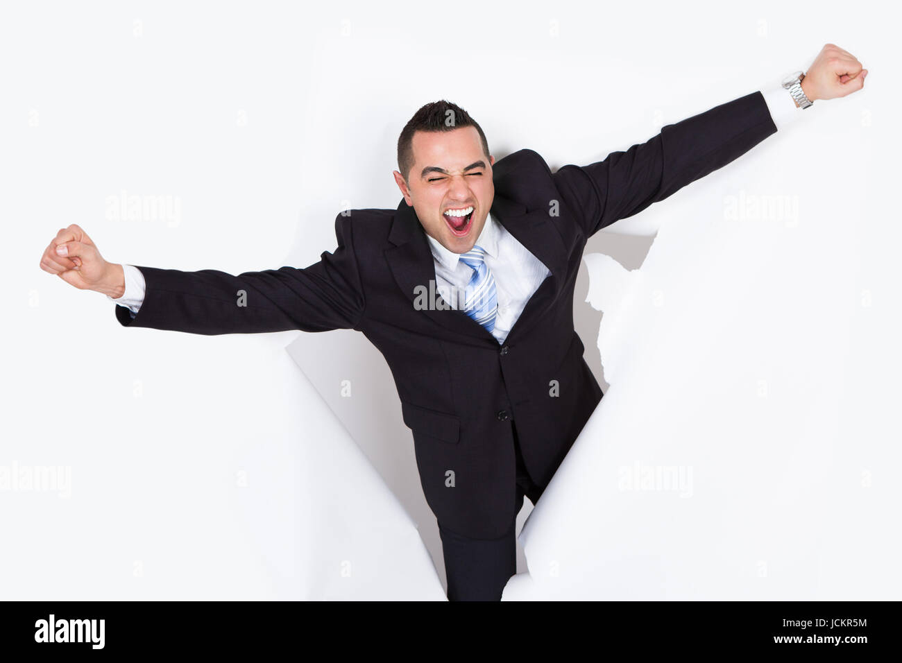 Successful businessman shouting while breaking through white paper wall ...