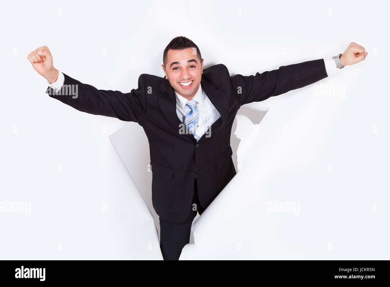 Successful businessman shouting while breaking through white paper wall ...