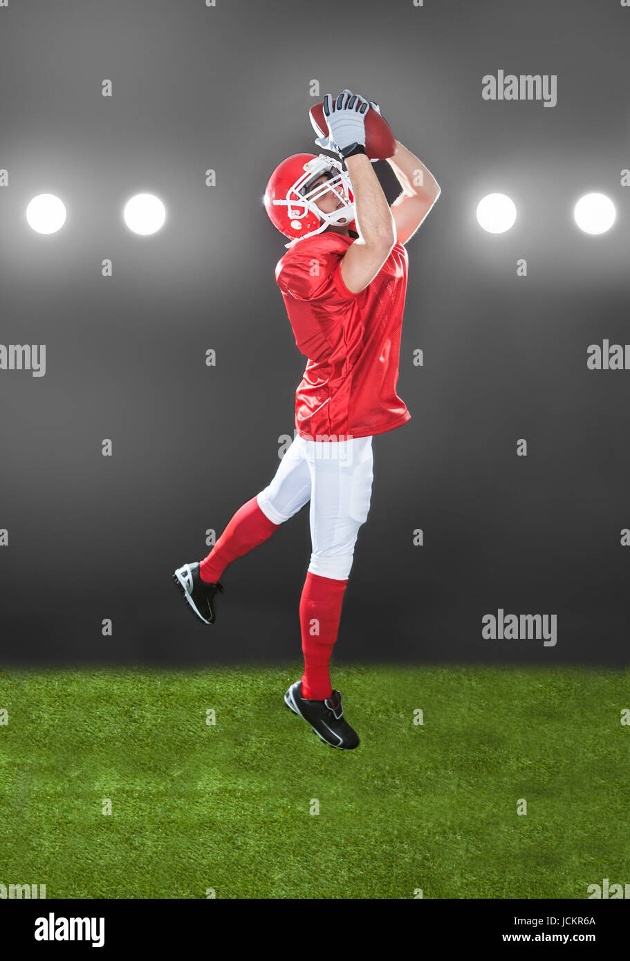 Full length of American football player jumping on field at night Stock ...