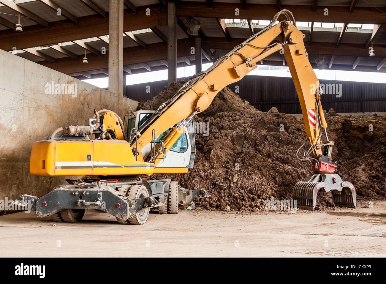 Bagger mit Greifarm vor einem großen Haufen brauner Erde in der ...