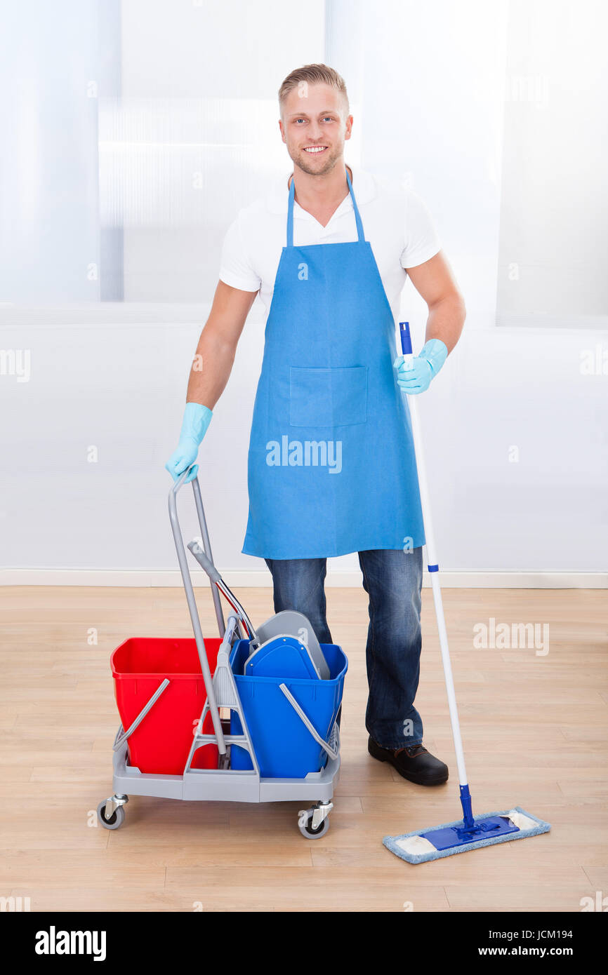 Janitor cleaning wooden floors with a mop and a cart with two buckets ...