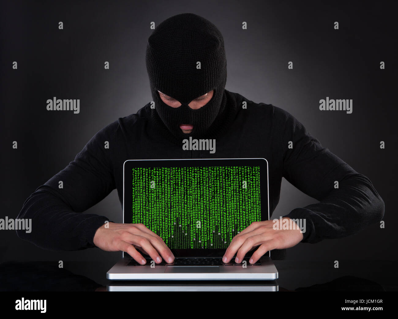 Hacker in a balaclava standing in the darkness furtively stealing data ...