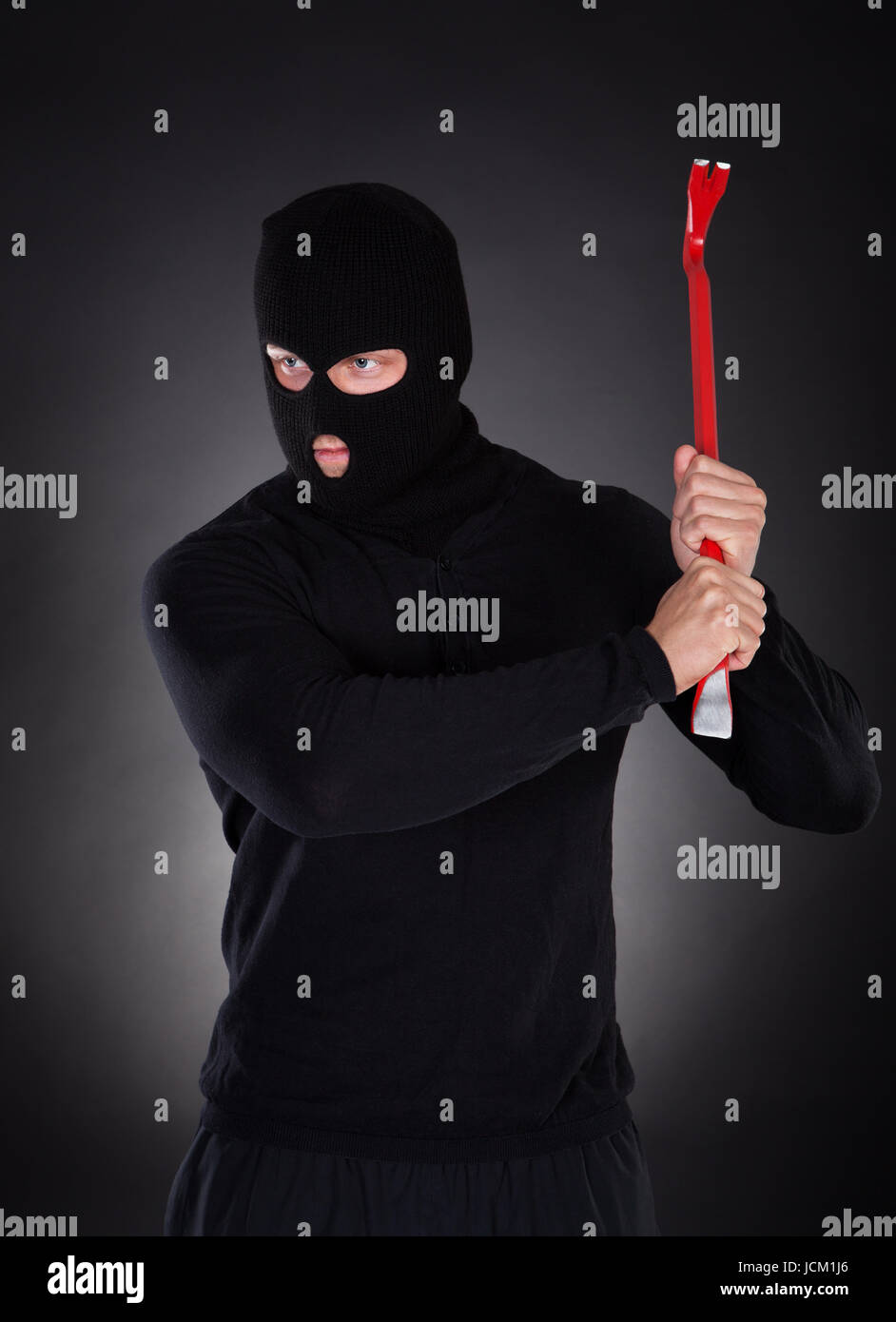 Masked thug or criminal with a crowbar raising it threateningly as he ...