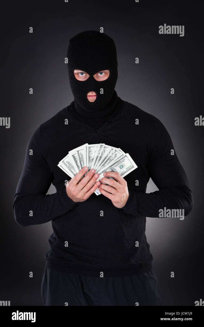 Criminal in a balaclava holding a fistful of money conceptual of the ...