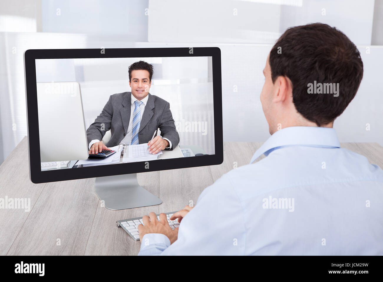 Rear view of businessman video conferencing with coworker on desktop PC ...