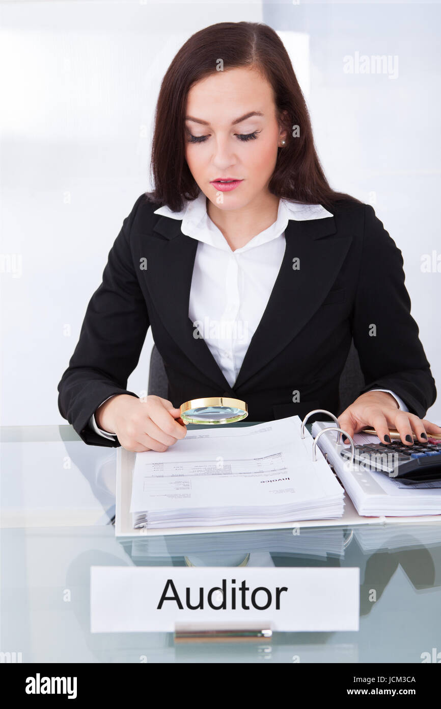 Young female auditor scrutinizing financial documents at desk in office ...