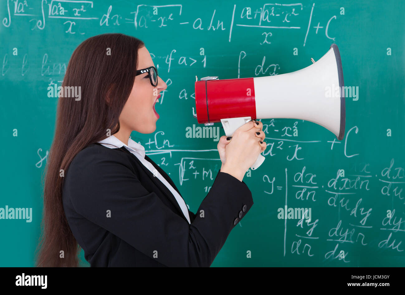 Angry young teacher shouting through megaphone against chalkboard in ...