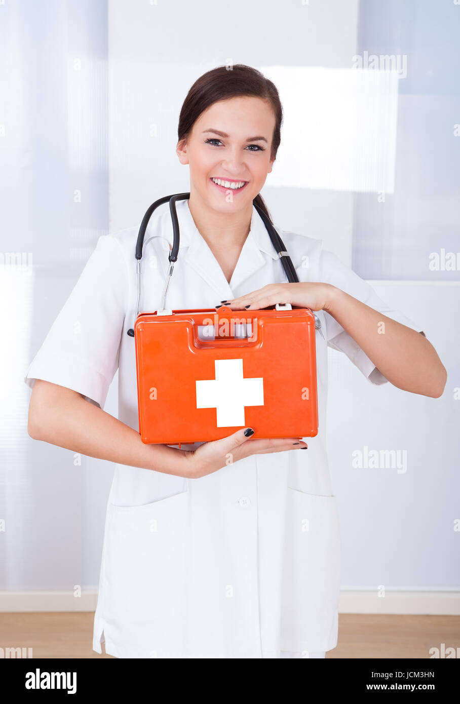 Portrait of happy young female doctor holding first aid box in hospital ...