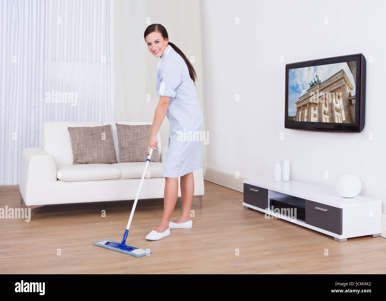 Full length portrait of young maid cleaning floor with mop at home ...