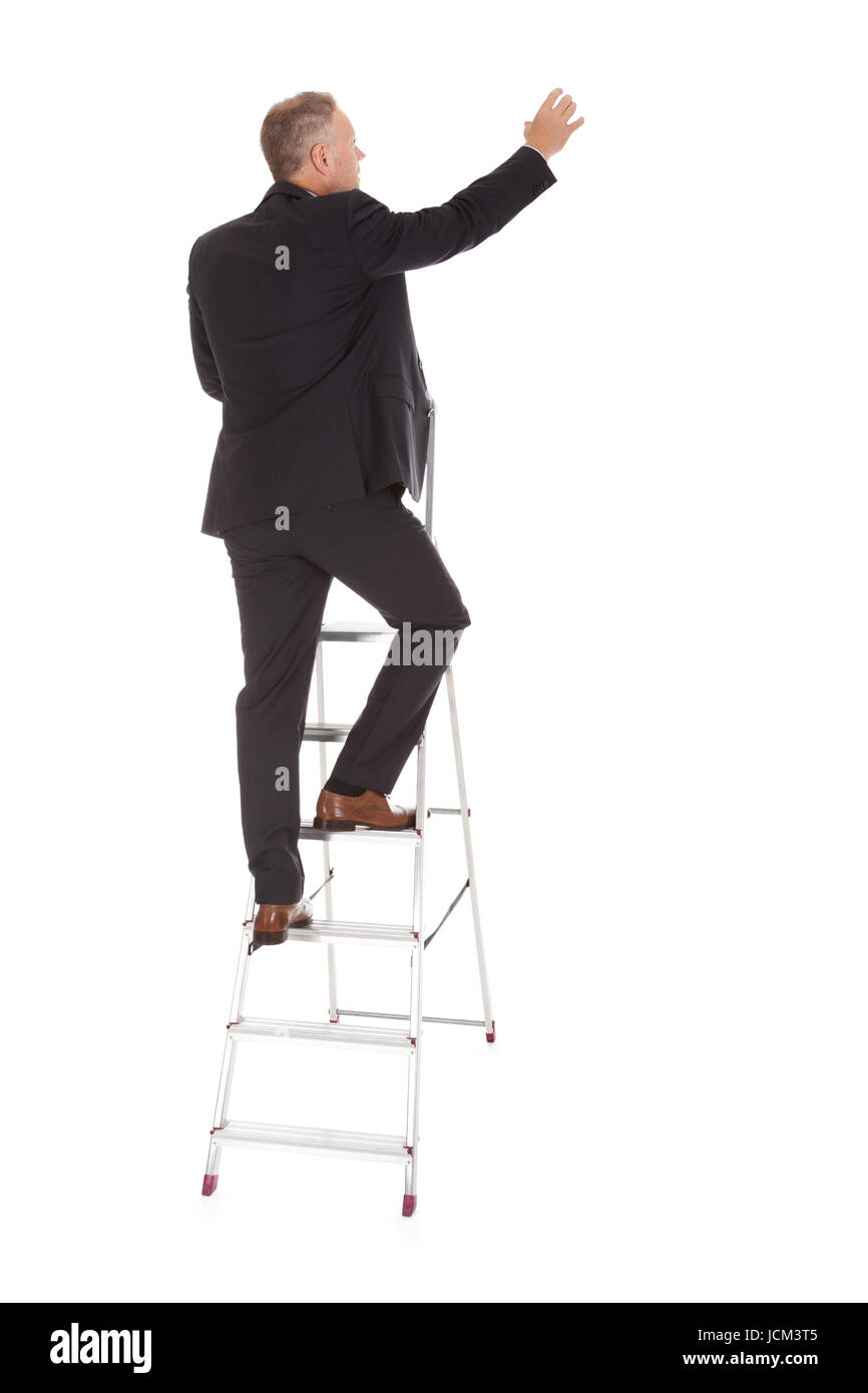 Full length rear view of mid adult businessman climbing ladder over ...