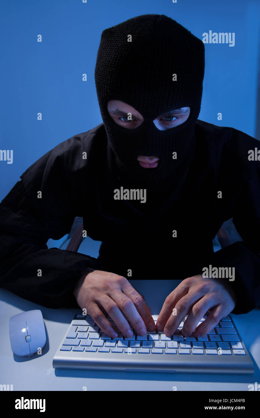 Criminal using computer to hack online account at table Stock Photo - Alamy