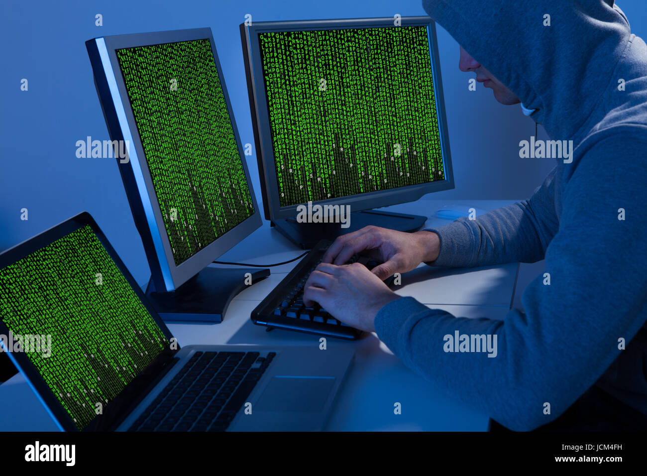 High angle view of hacker in hooded jacket using computer at table ...