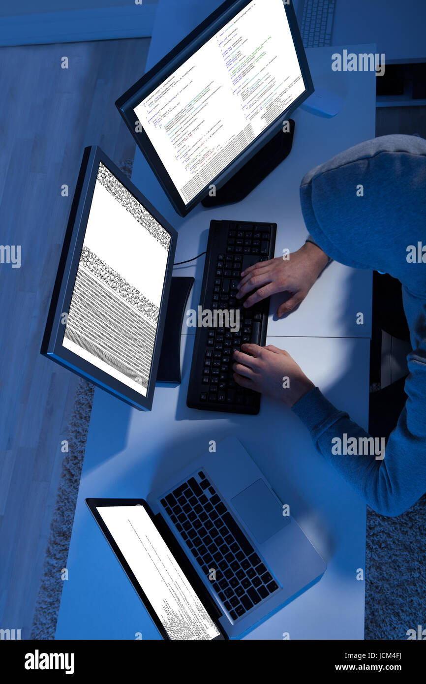 Side view of hacker using multiple computers to steal data at table Stock Photo - Alamy