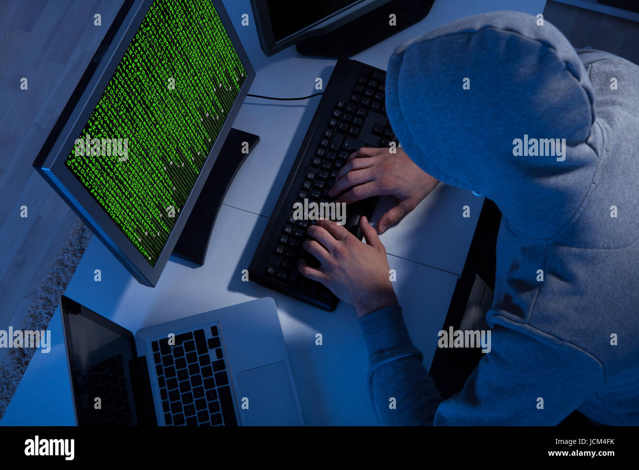 High angle view of hacker in hooded jacket using computer at table ...