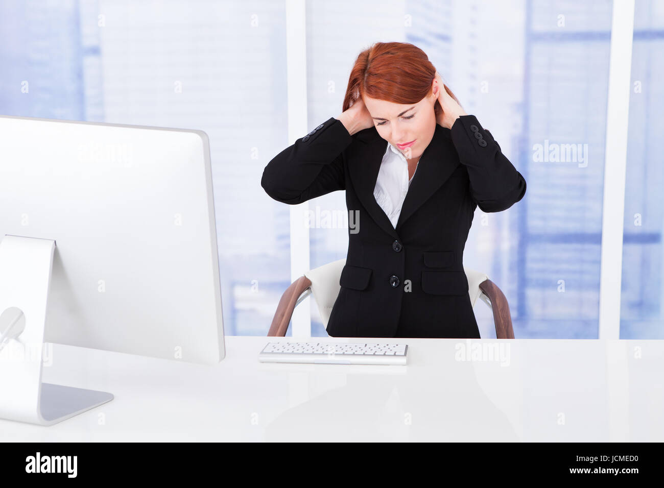Young businesswoman having neck pain while working at computer desk in ...