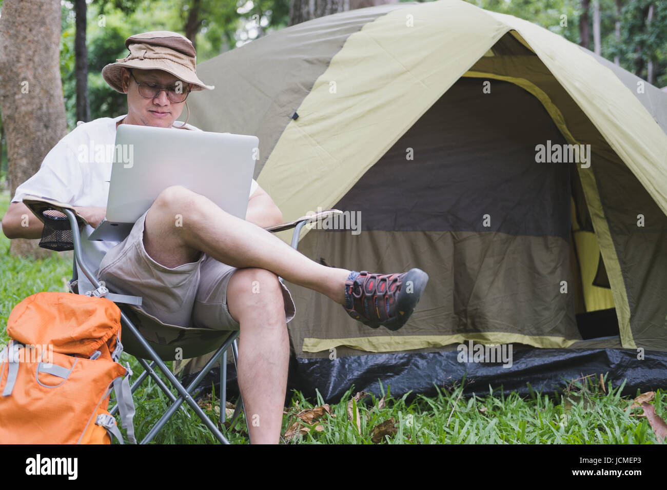 young asian man tourist sitting on chair and using laptop in front of ...