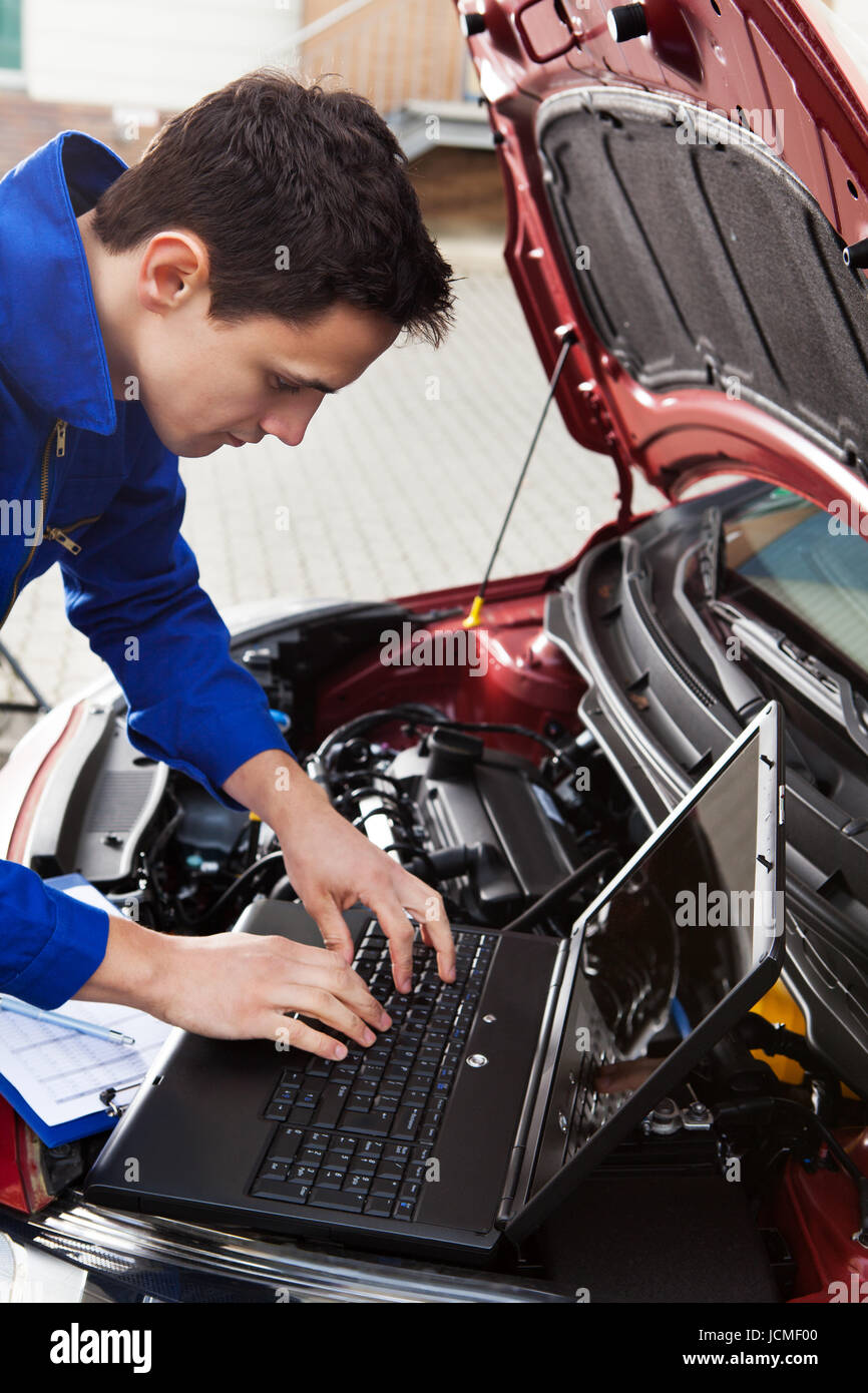 Side view of young mechanic using laptop while repairing car on street ...