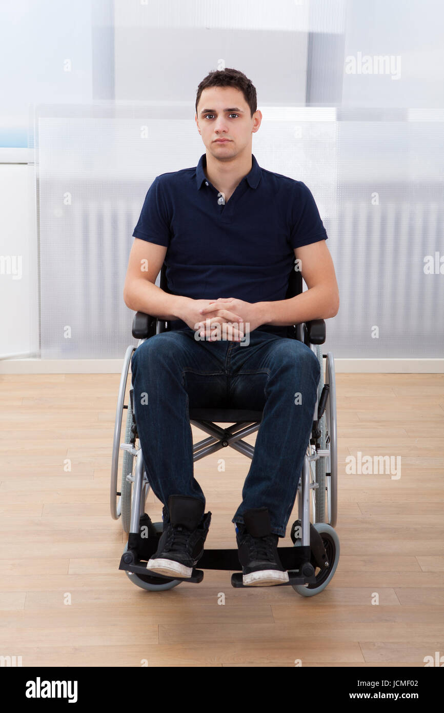 Full length portrait of young handicapped man sitting on wheelchair at ...