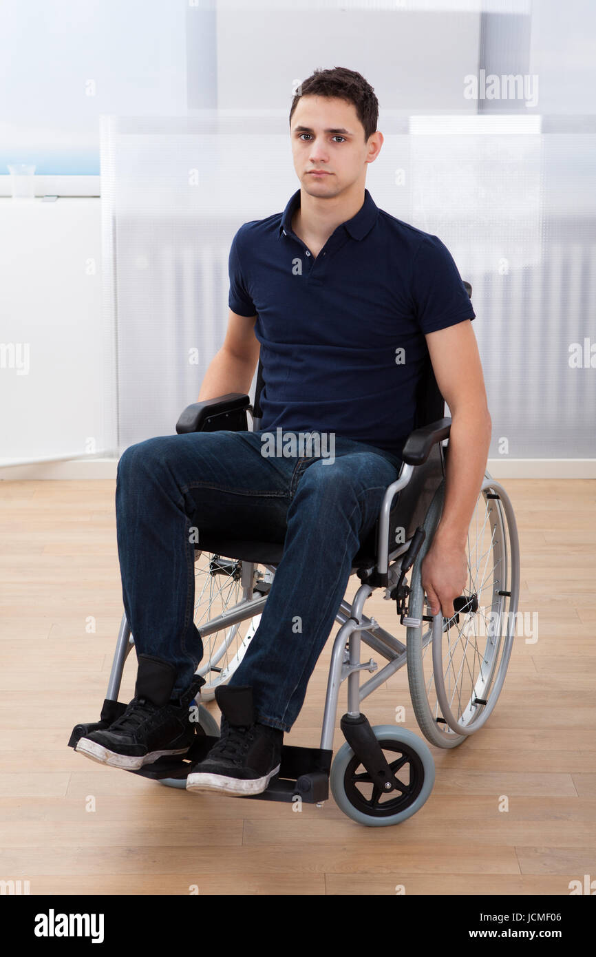 Full length portrait of young handicapped man sitting on wheelchair at ...