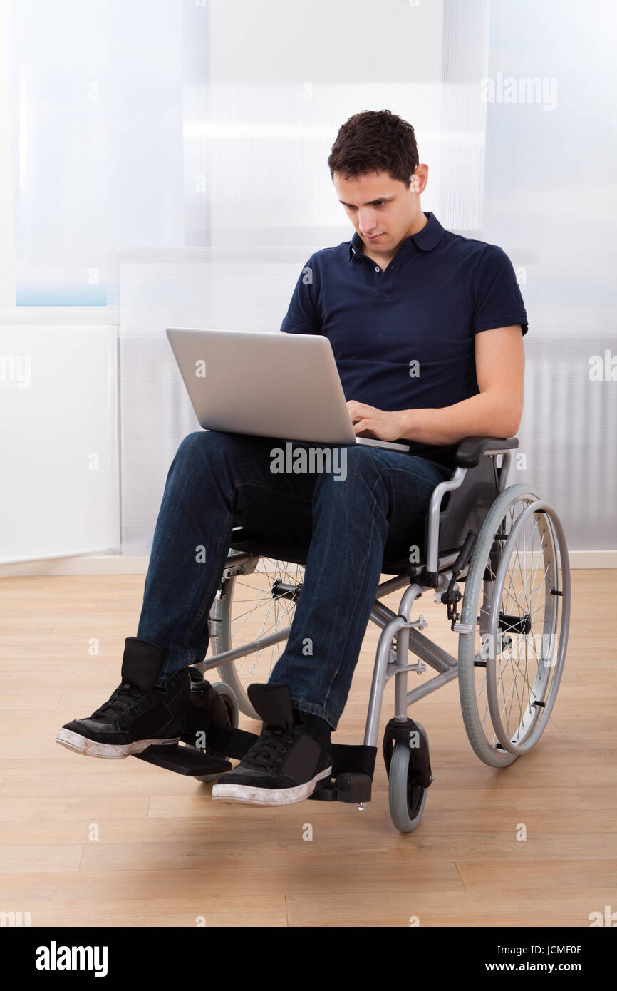 Full length of young handicapped man using laptop while sitting on ...