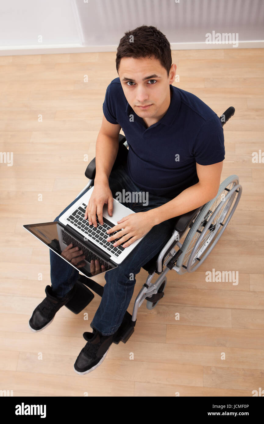 Full length of young handicapped man using laptop while sitting on ...