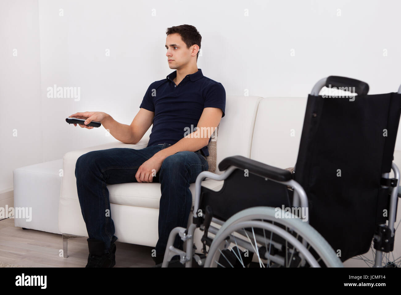 Young handicapped man using remote control while watching television in ...