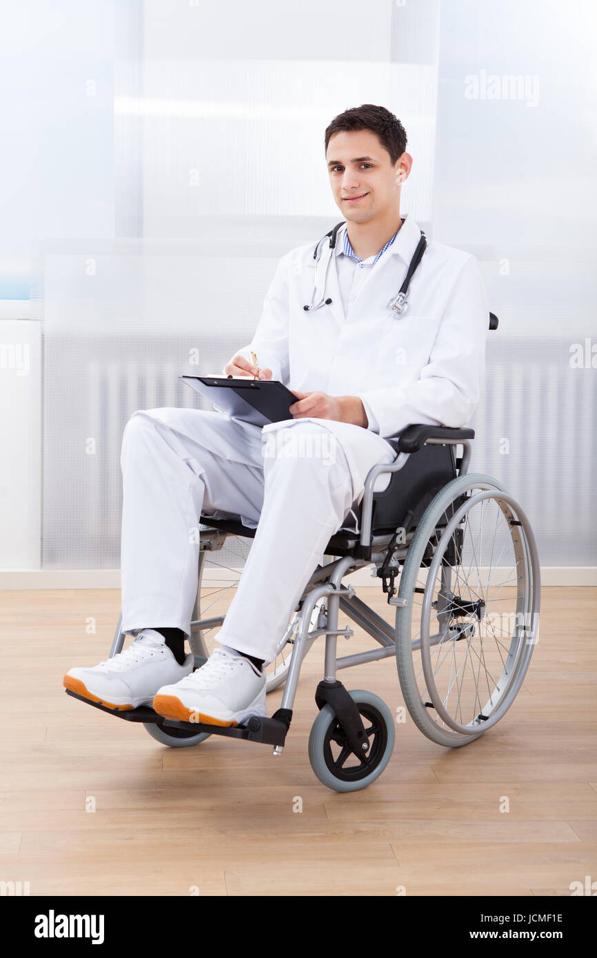Full length portrait of handicapped doctor witting on clipboard while ...
