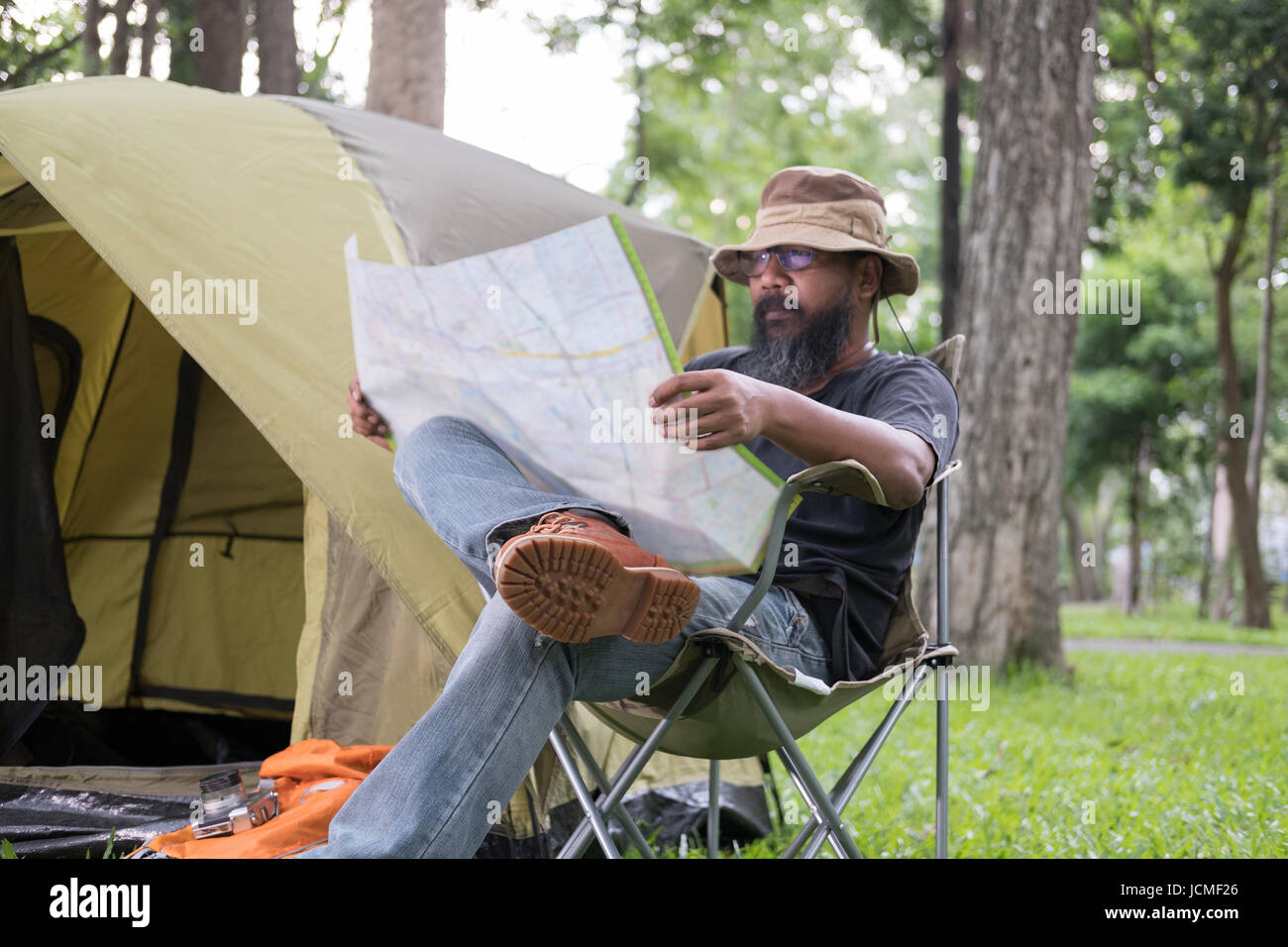 man tourist sitting on chair and reading map in front of tent at ...
