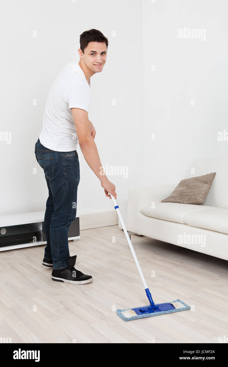 Full length of young man mopping floor at home Stock Photo - Alamy