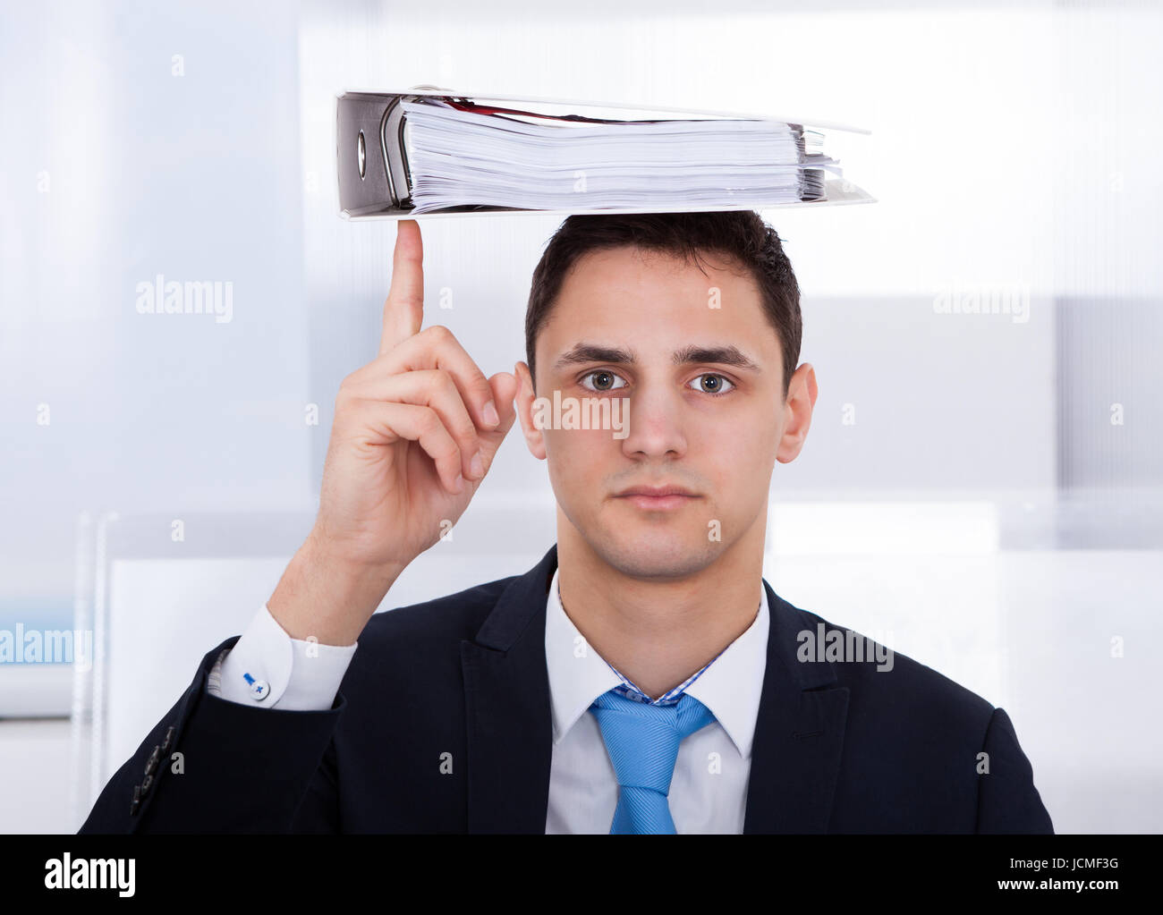 Portrait of businessman balancing binder on head with index finger in ...