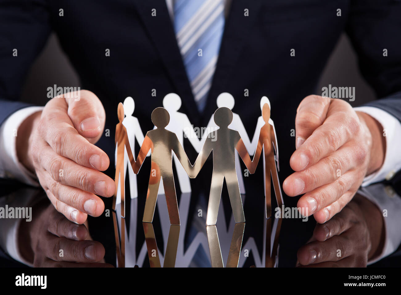 Midsection of businessman's hands protecting team of paper people on ...