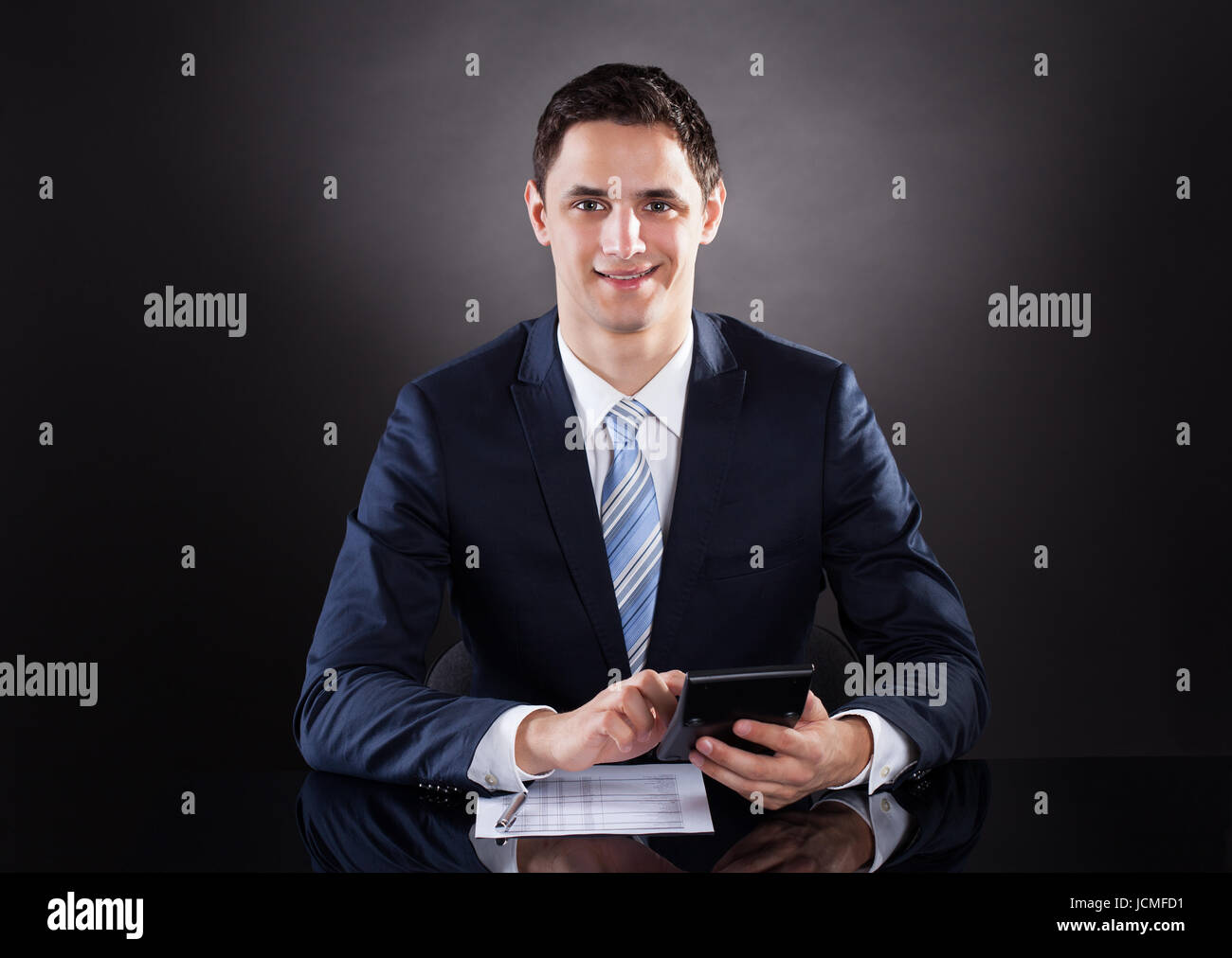 Handsome businessman calculating finance at desk against black ...